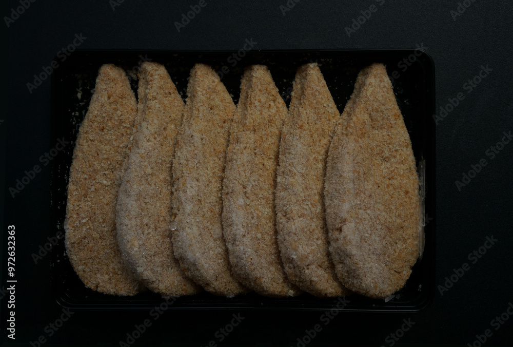 Raw frozen chicken cutlets in plastic black container isolated on dark ...