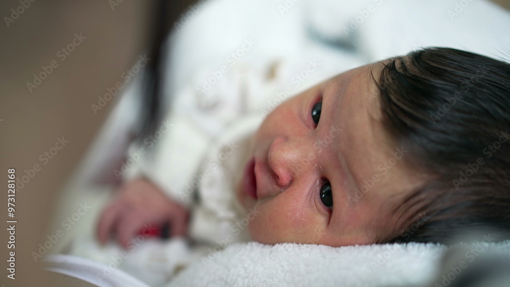 Newborn baby gazing up with bright eyes, resting peacefully in a ...