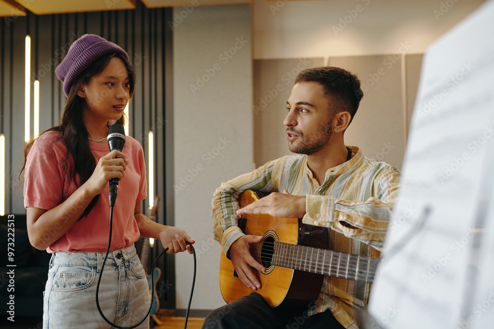 Girl holding microphone while man plays guitar in music studio. Both ...