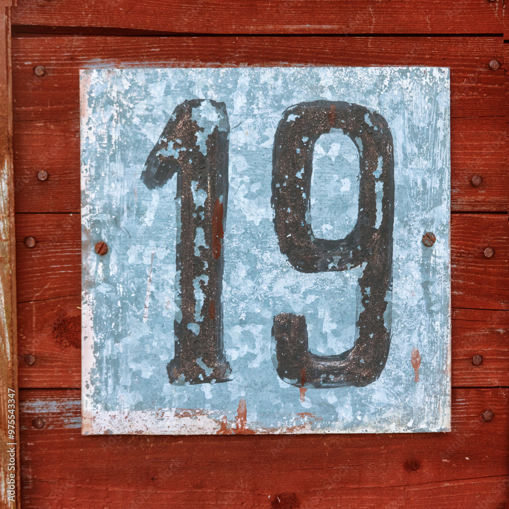 A faded number 19 on a square metal plaque. The numbers are hand ...