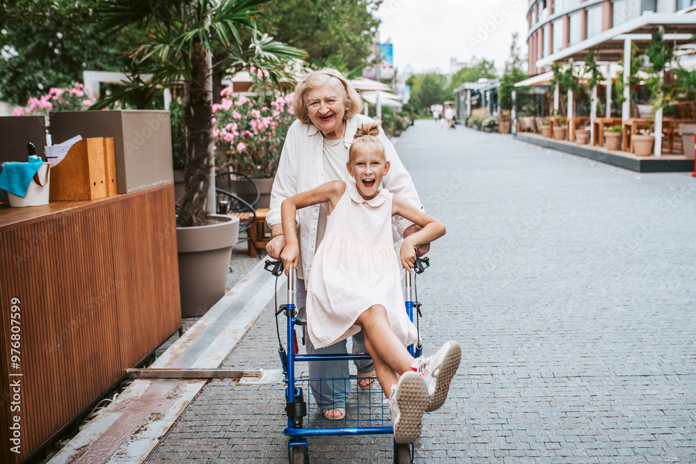 Girl sitting on rollator, grandma pushing her, laughing. Granddaughter ...