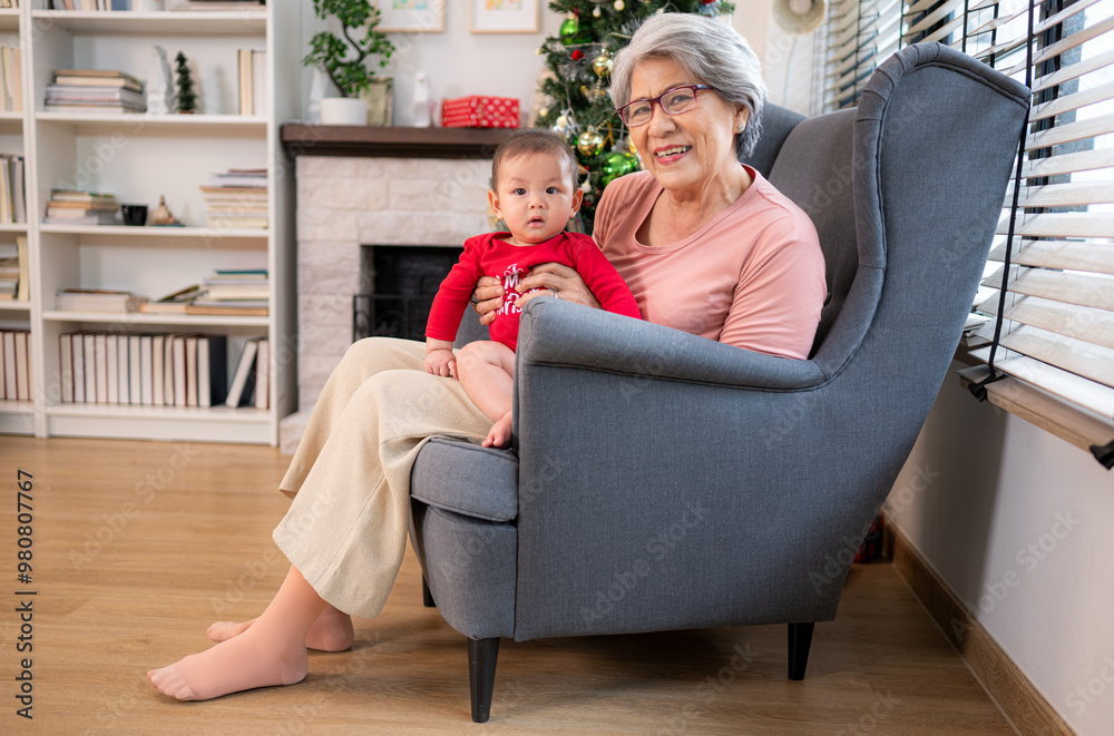 Grandma is sitting in an armchair, holding her infant grandson ...