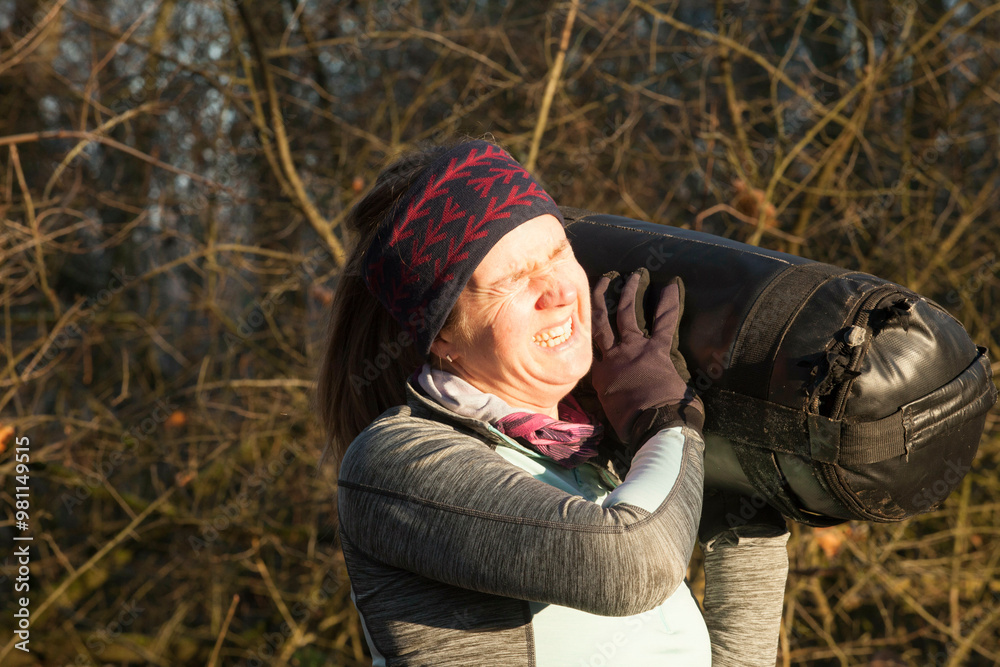 Woman grimacing as she carries a heavy tire on her shoulder during an ...