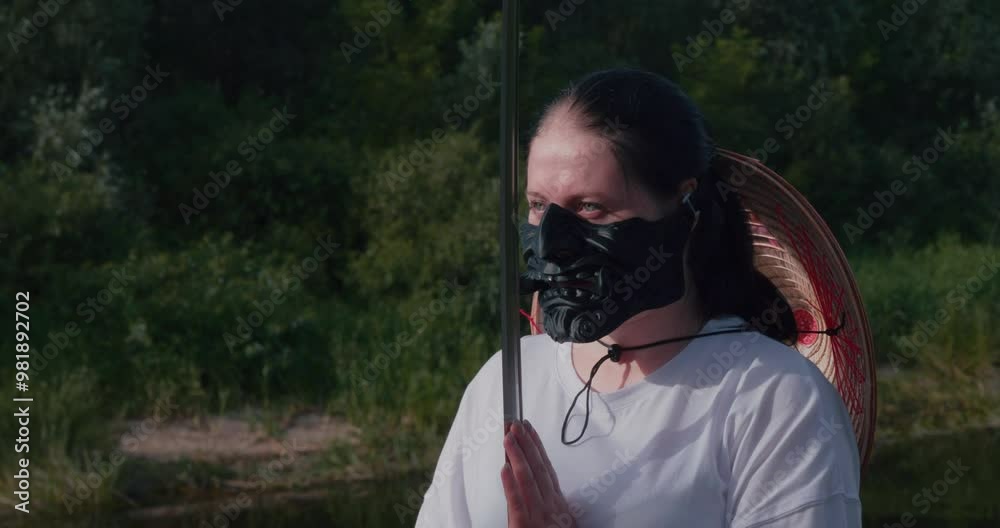Close-up. Holding a katana in front of her, a masked woman meditates ...