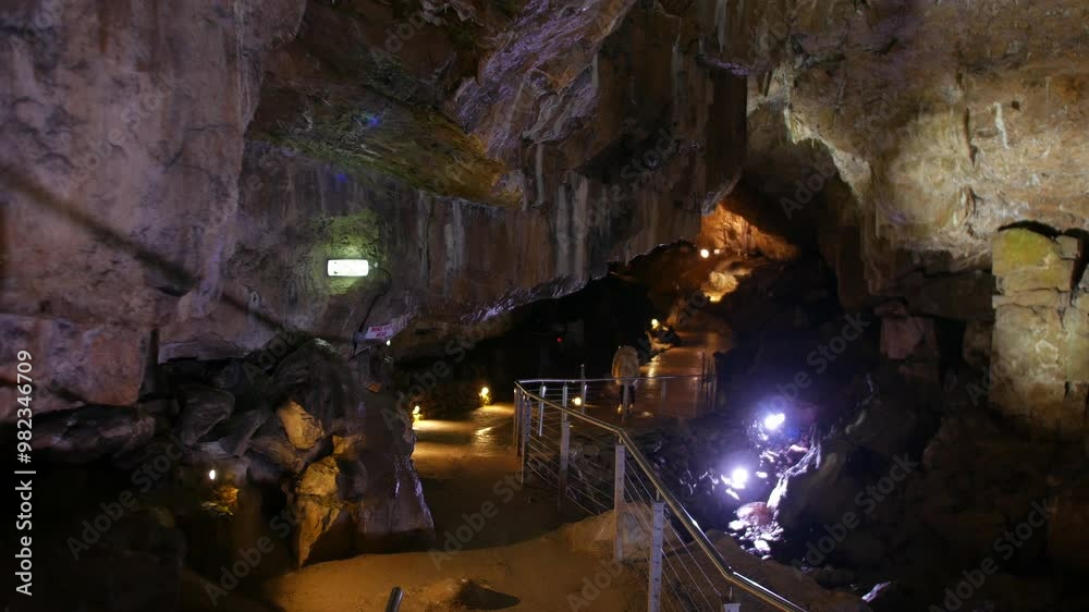 A dark cave features a winding path with railings, steps guiding ...