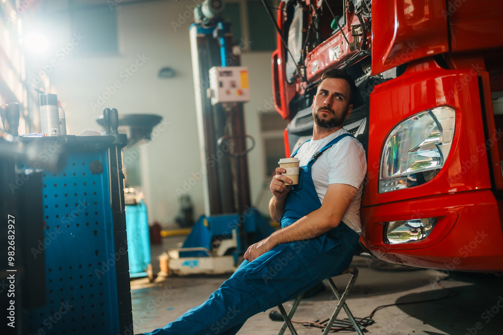 Mechanic in blue overalls sits relaxed with a cup of coffee next to a ...