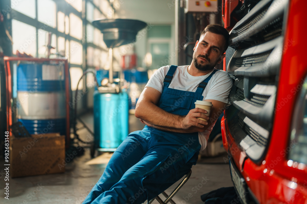 Mechanic in blue overalls sits relaxed with a cup of coffee next to a ...