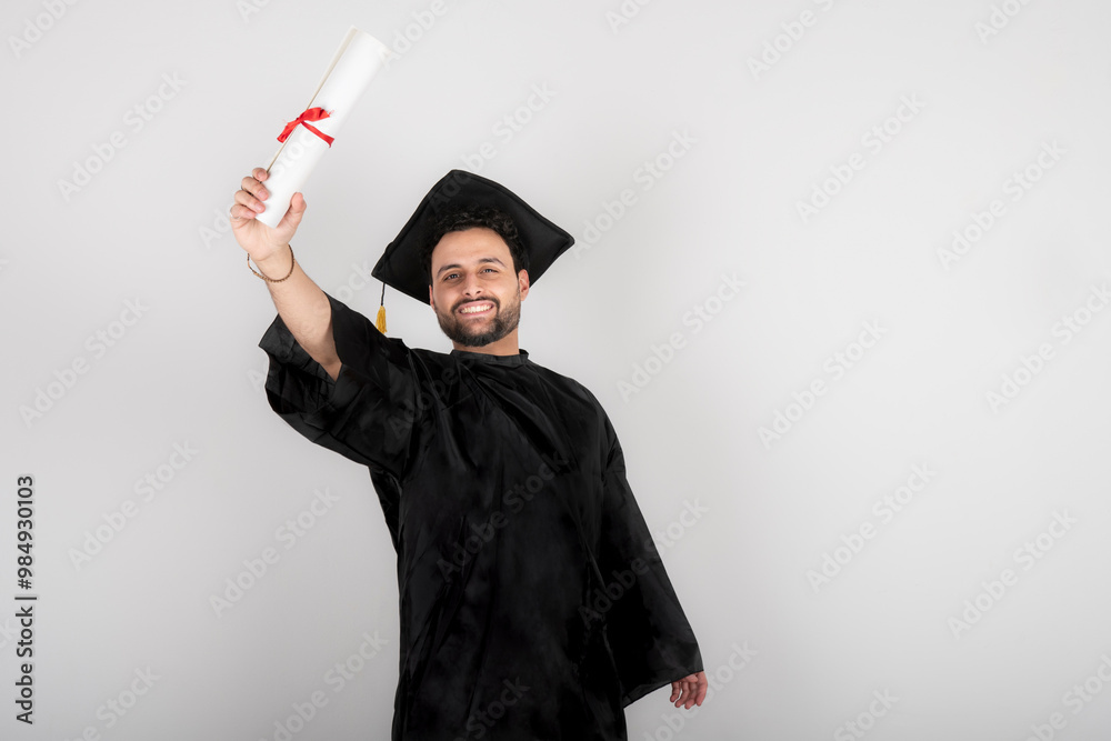 Recent graduate man, dressed in cap and gown, showing off his degree ...