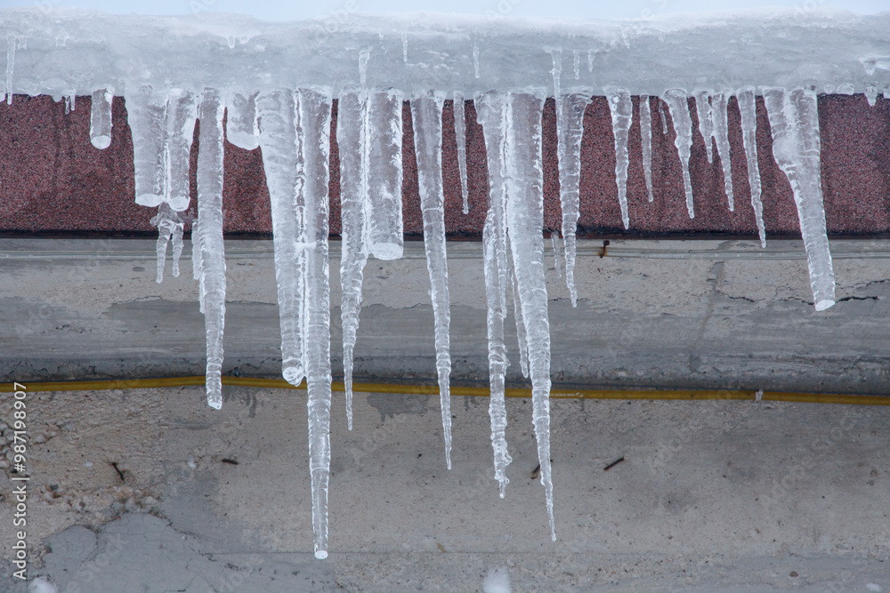 Gleaming icicles hang from a roof edge, contrasting against red ...
