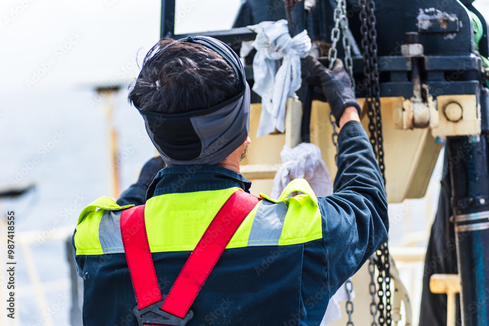 A deck crew member of a merchant ship working at height, equipped with ...