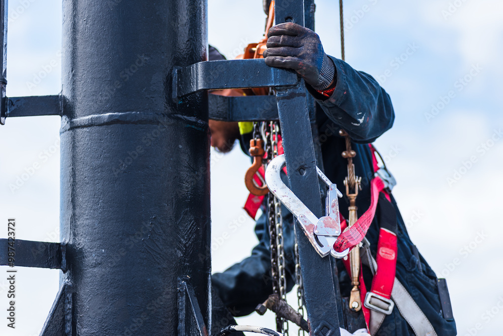 A deck crew member of a merchant ship working at height, equipped with ...