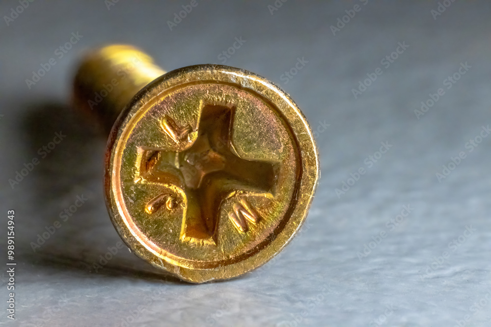 A close-up of a yellow Phillips-head screw head. The screw head is ...