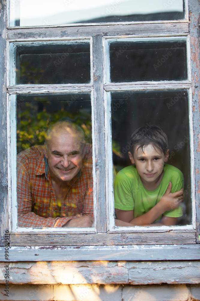Grandfather and grandson looking out of the window of a village house ...