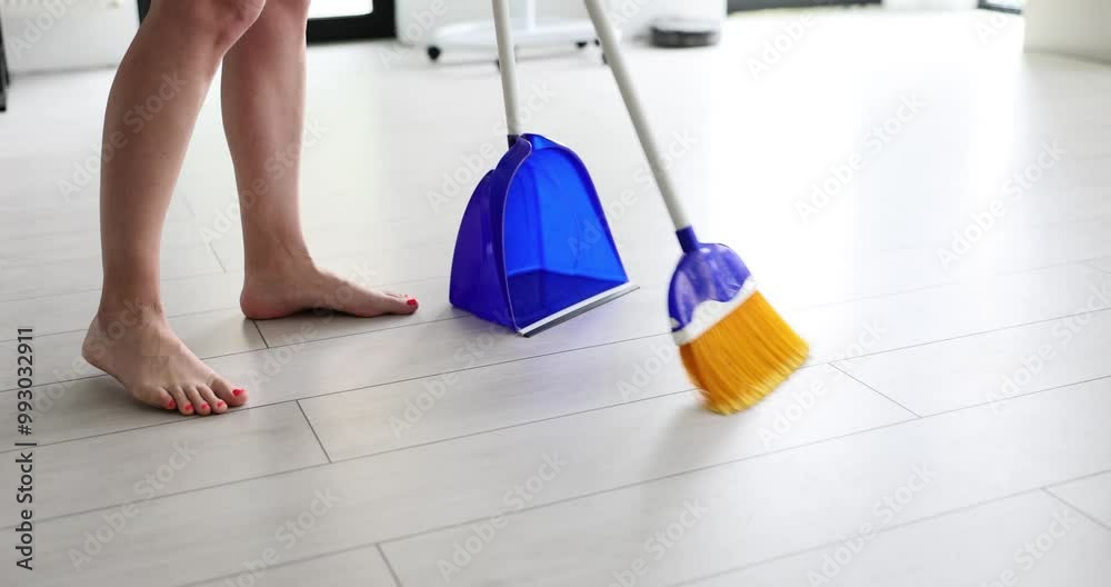 Barefoot female person sweeps light wooden floor using broom and ...