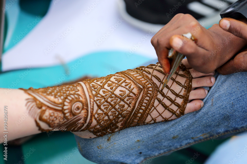 an artist applying intricate henna (mehndi) designs to a person's hand ...