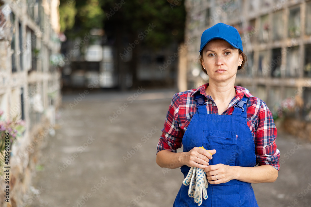 Young female cemetery employee stands with cloth work gloves in hands ...