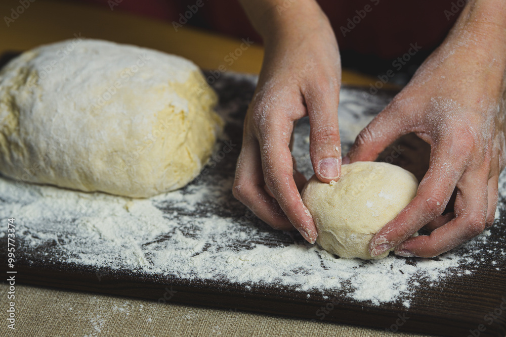 Women's hands forming buns of dough on a kitchen board, warm photo of ...
