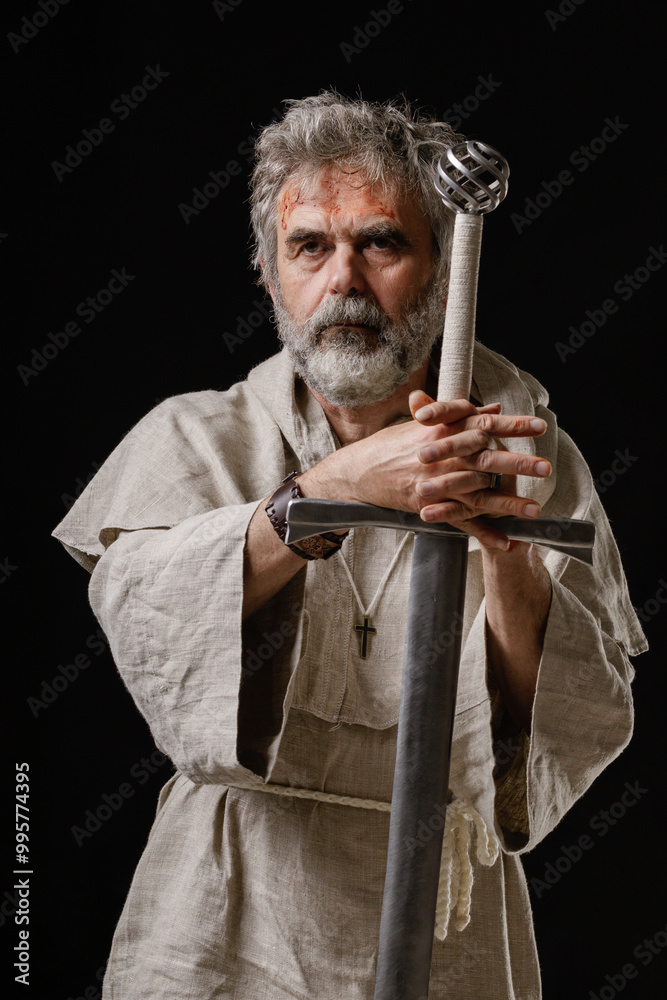 An old knight monk with a bloody forehead leans on his large two-handed ...