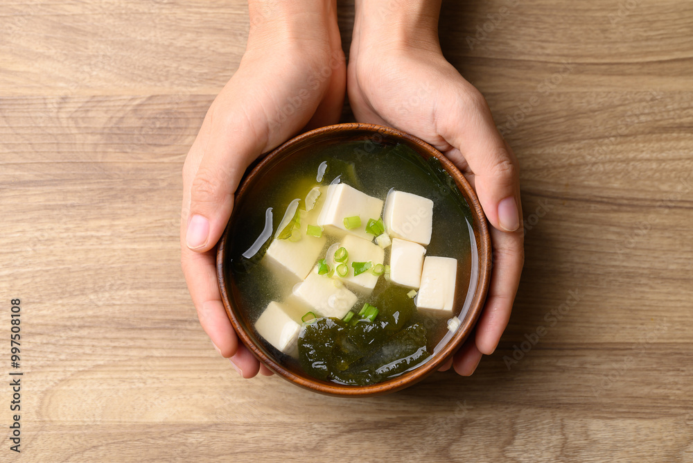 Miso soup with tofu, wakame seaweed and spring onion in bowl with hand, Traditional Japanese ...