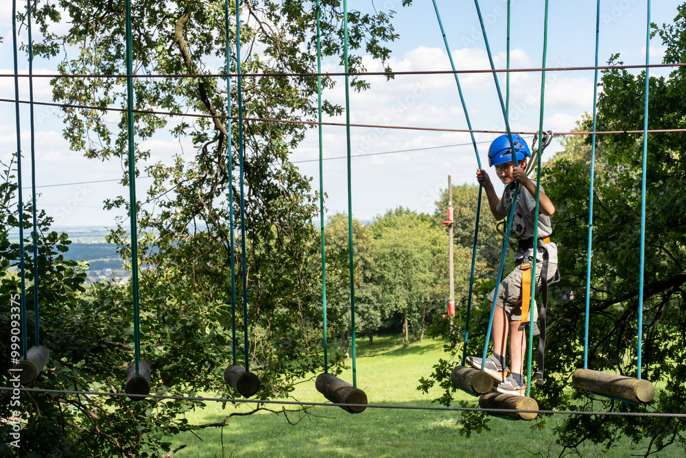 Young boy balancing on a rope bridge in an outdoor adventure park ...