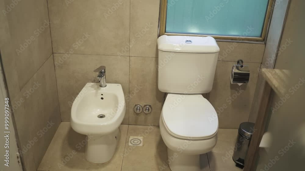 A slow-moving shot captures a hotel bathroom featuring both a bidet and ...