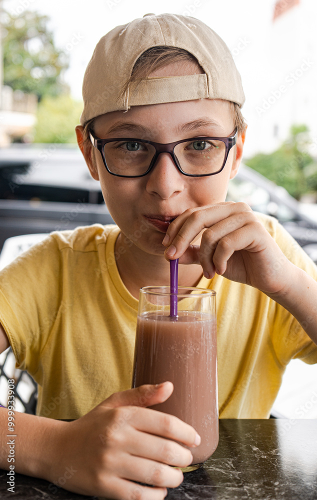 Smiling teenage boy wearing a baseball cap sitting in a cafe drinking a ...