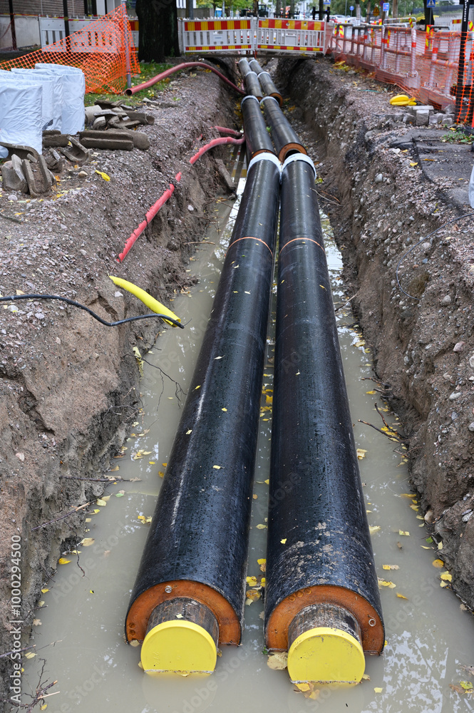 Two large insulated pipes are visible in a trench filled with water ...