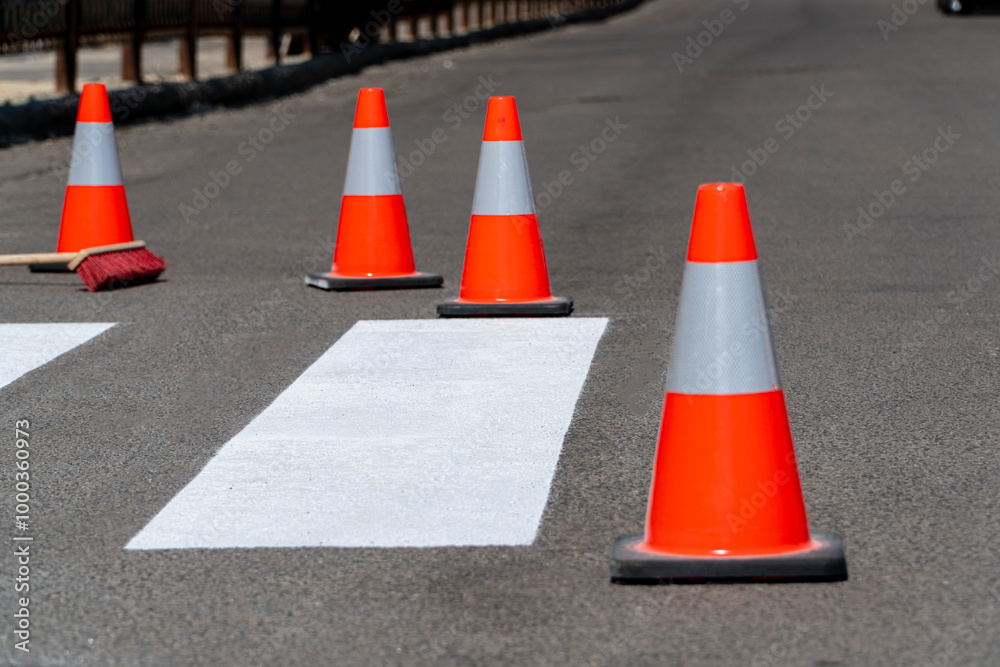 Bright orange traffic cones are placed along a newly marked crosswalk ...