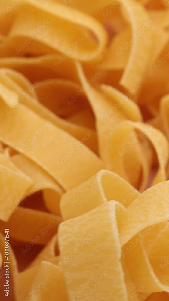 a close-up of raw, flat, wide noodles or pasta ribbons, rotation in ...