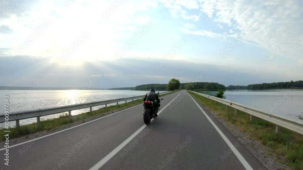 Biker riding on modern sport motorbike through road near lake ...