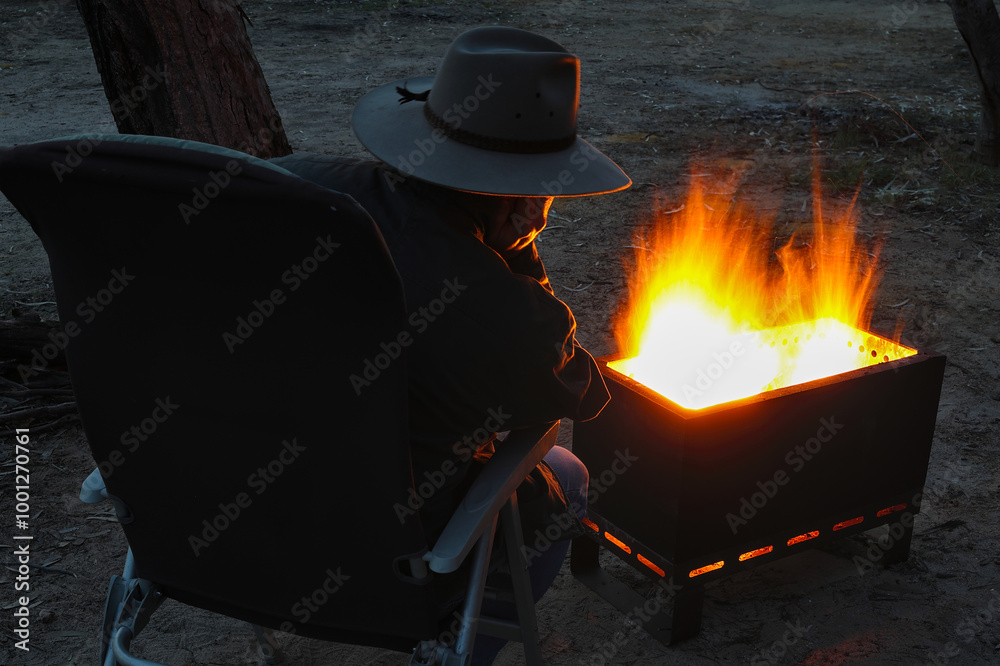 Semi dark. Man, looking away, towards flames in smokeless fire pit ...