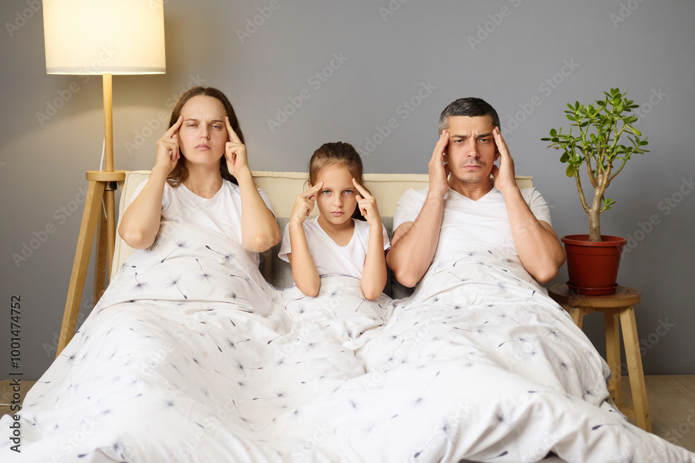 Sad upset family lying together in bed with little girl grimacing from ...