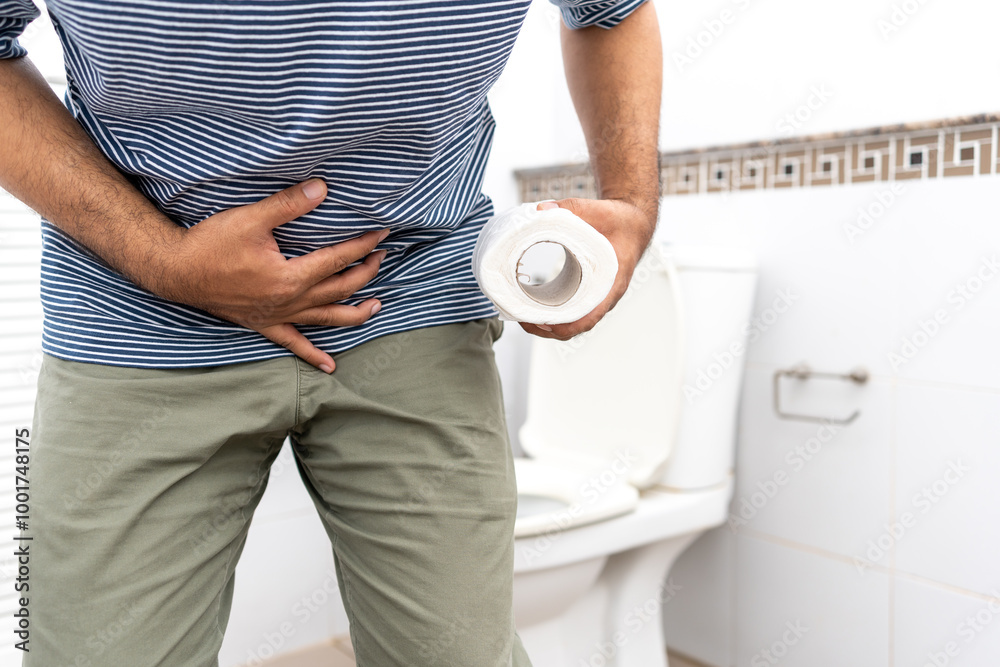 Male suffers from diarrhea holds toilet paper roll in front toilet bowl ...