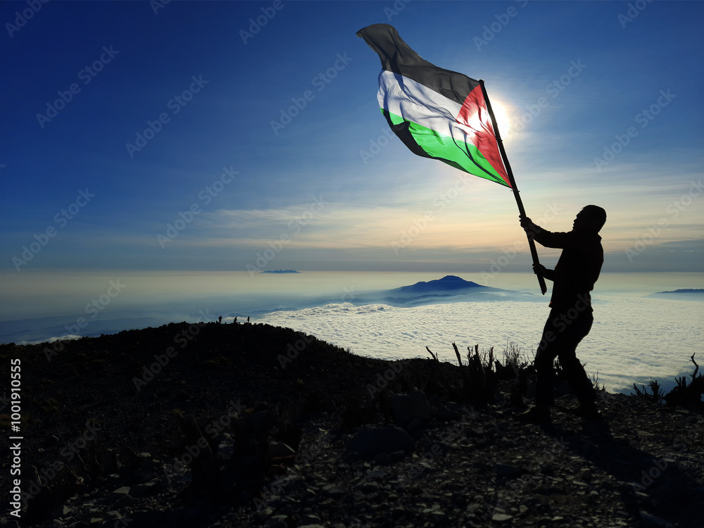 man raising the flag of palestine on the top of the mountain ...