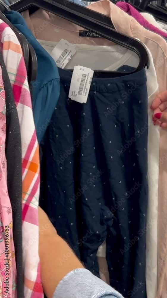 A young poor girl browses the racks of clothes in a thrift store. Stock ...