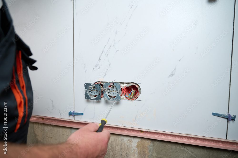 Professional electrician installing electric socket into the wall using ...