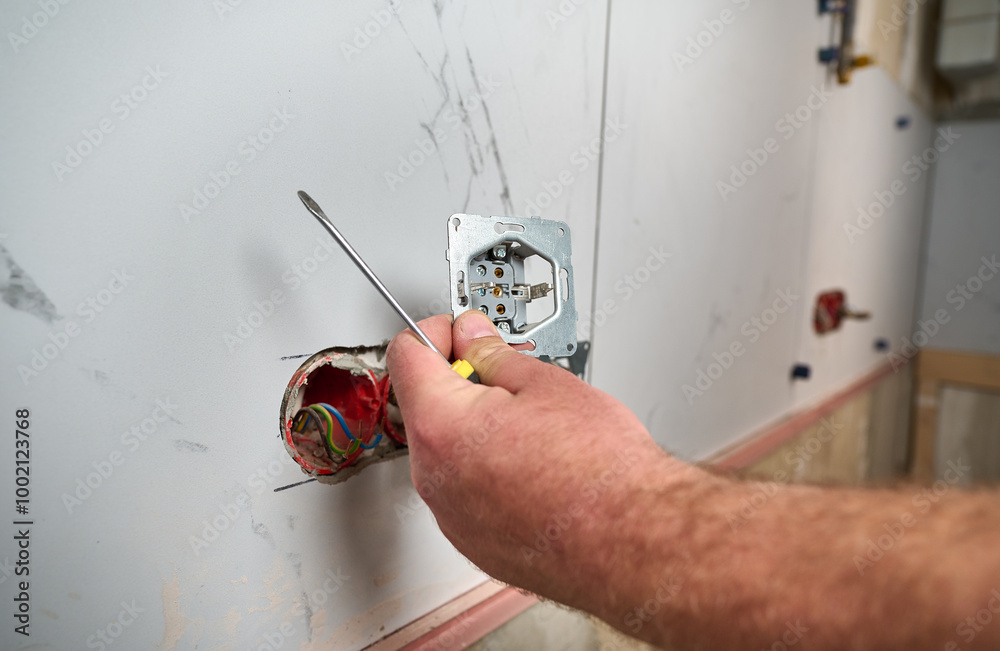 Professional electrician installing electric socket into the wall using ...