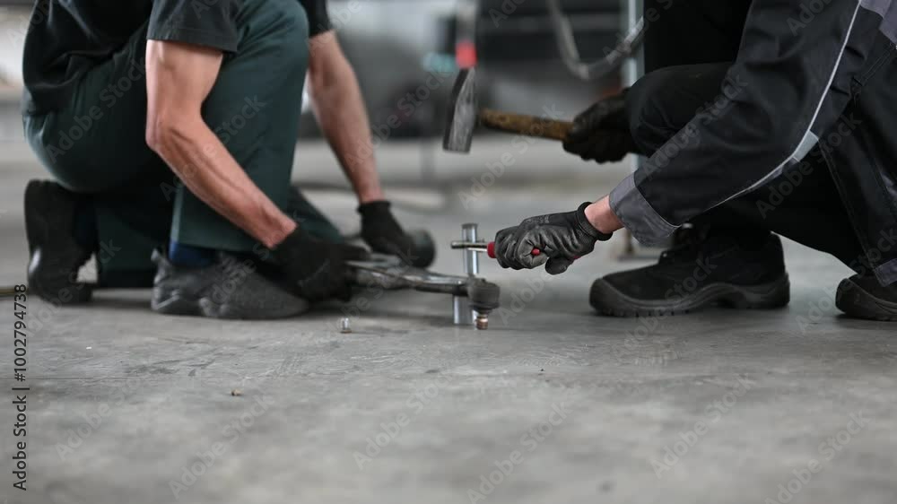 Two mechanics wearing work clothes and gloves are crouched down working ...