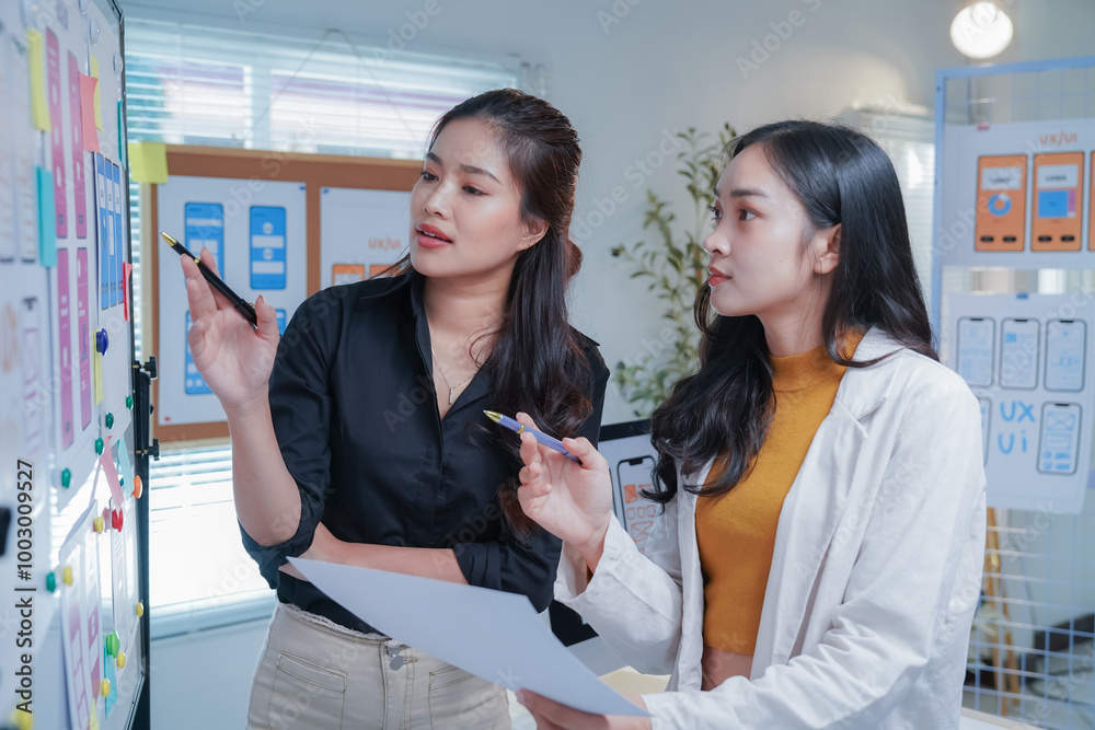 Two Asian Ui Ux Web Designers Are Reviewing Mobile App Interface Designs And The User Journey Of