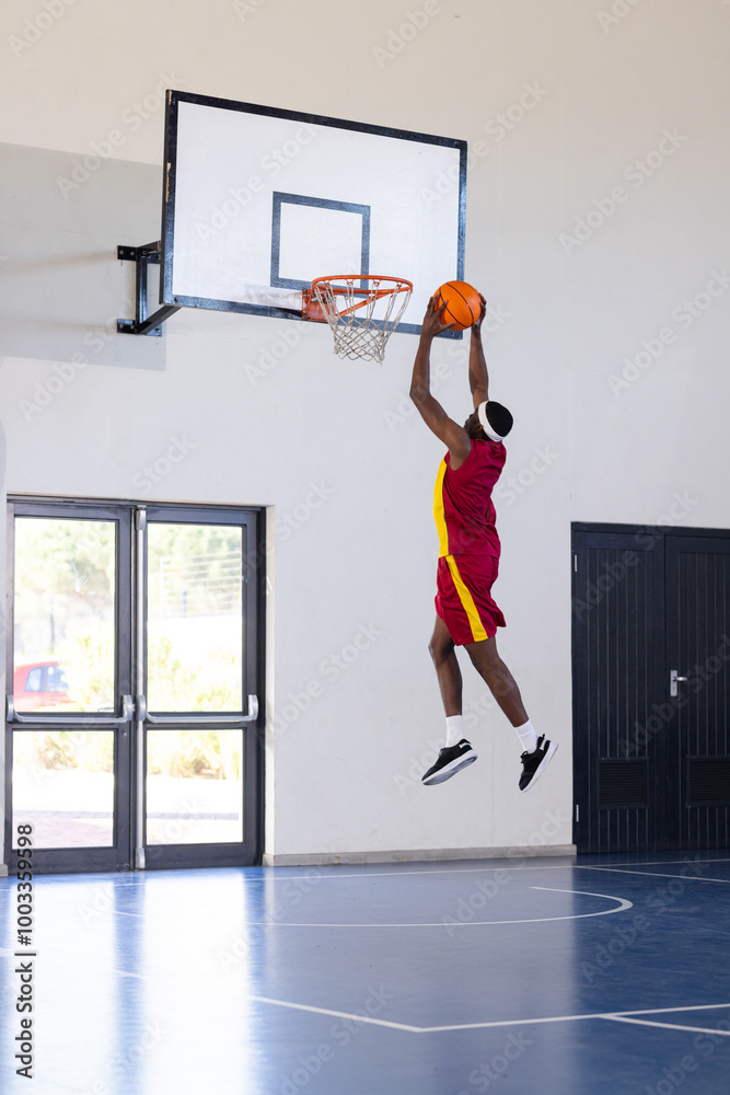 Dunking basketball, athlete in red uniform jumping high in indoor court ...