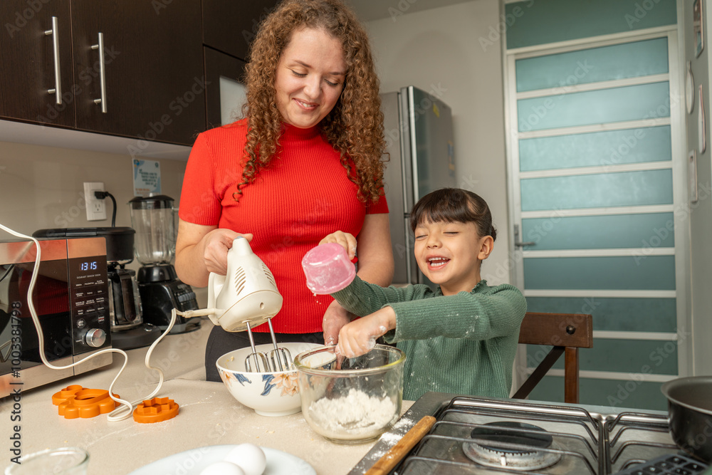 Mother using a hand mixer while her smiling daughter adds flour with ...