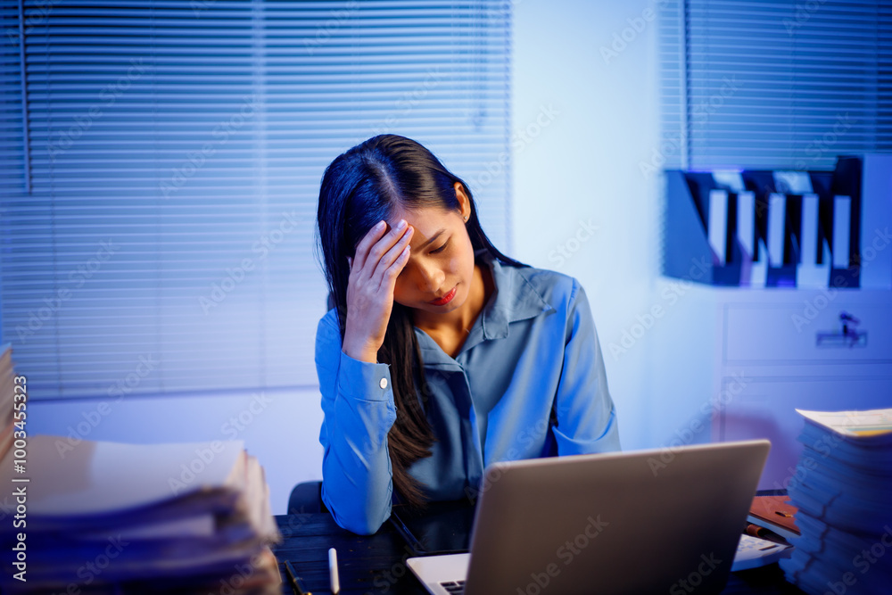 Asian businesswoman works late into the night in her office, documents ...