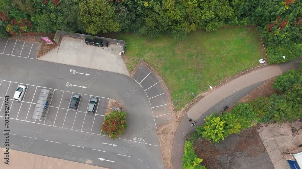 An aerial view of a parking lot with cars and surrounding greenery. The ...
