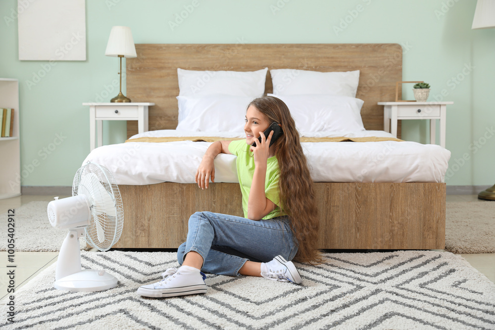 Teenage girl sitting on floor and using mobile phone near electric fan ...