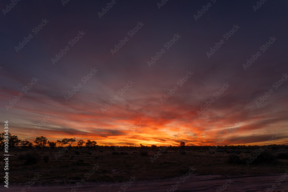 A fiery orange sunset lights up the sky and clouds with silhouettes of ...