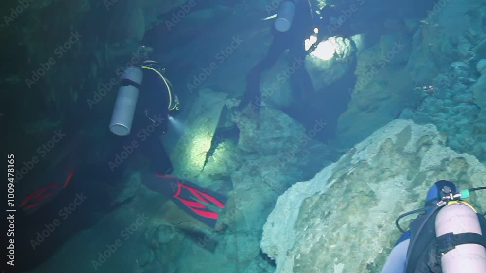 Three people are scuba diving in a cave. The cave is dark and the water ...