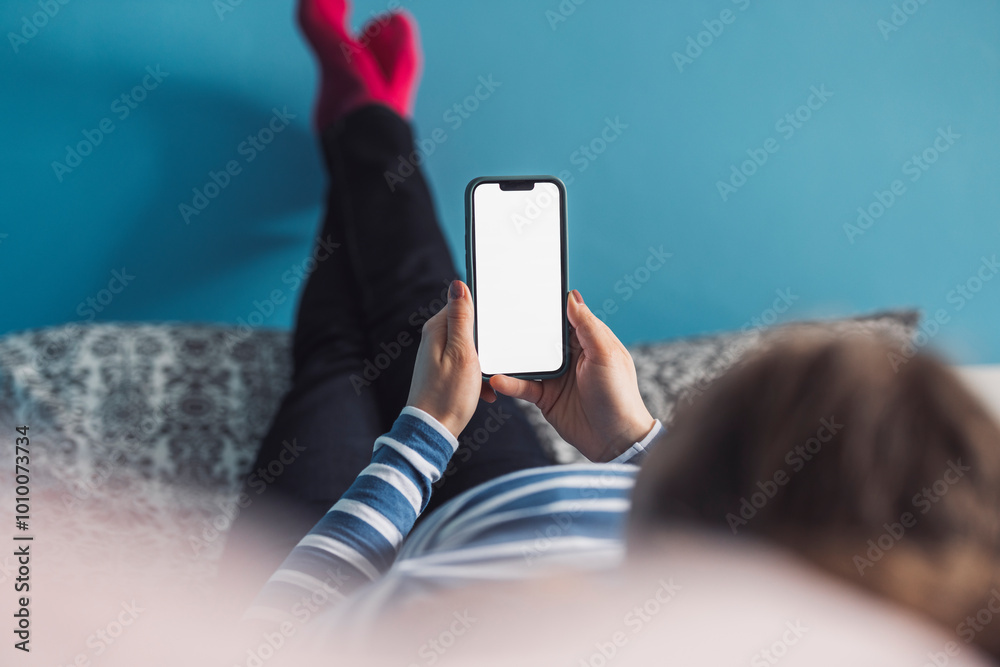 Closeup of hands holding phone with a white screen. Woman lying on bed ...