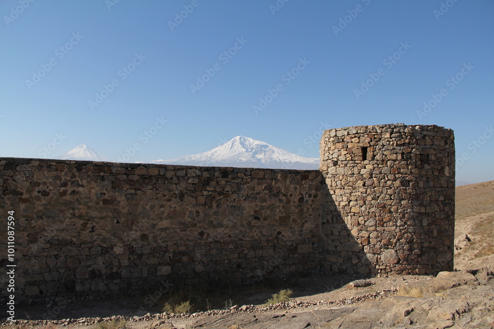 This image shows an ancient castle ruin with a snow-capped mountain in ...