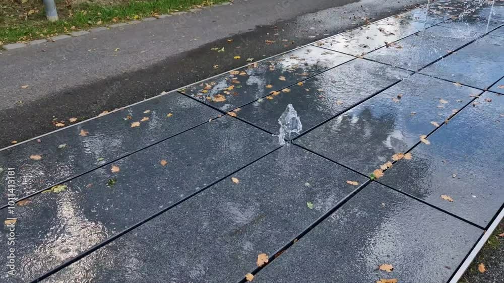 square granite paving stacked in a strip in sidewalk, water sprays with ...