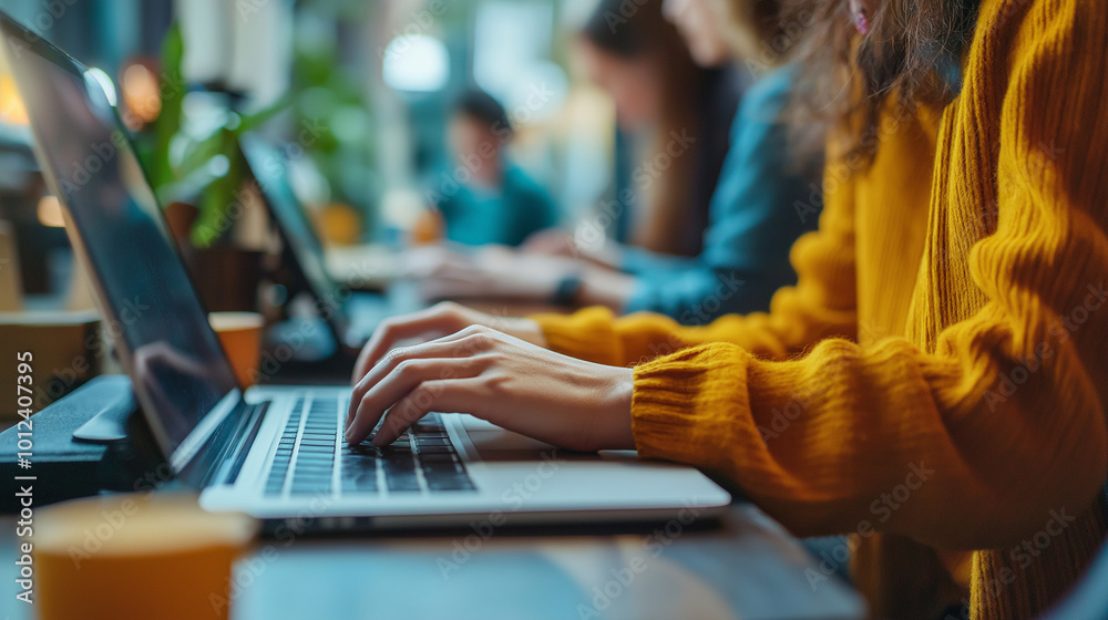 Young Employee Typing on a Laptop During a Team Meeting, Focusing on ...